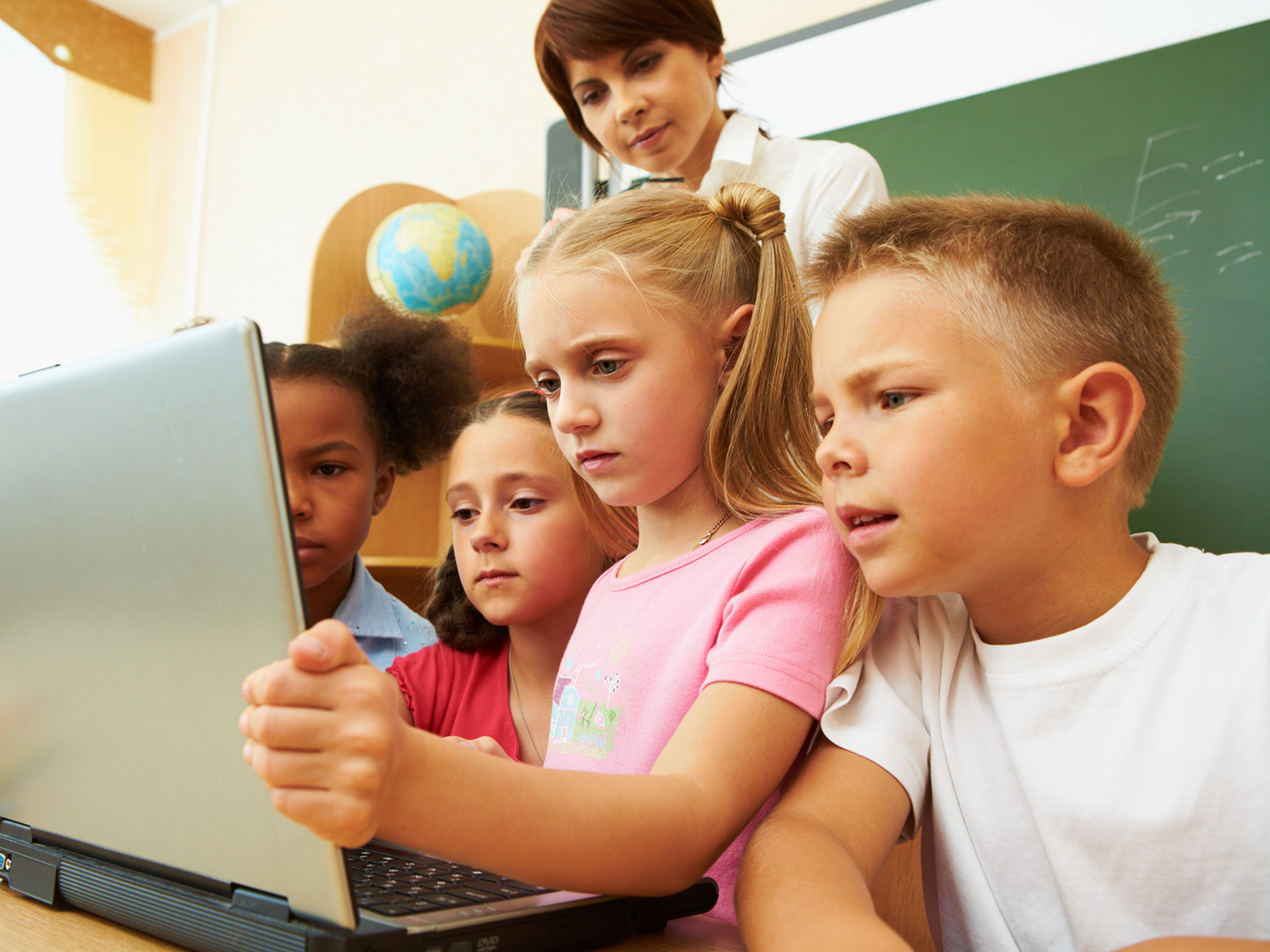 Kids in classroom huddled around laptop_1440x1080 – World Mosaic